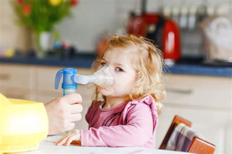 집에서 분무기로 흡입을 하는 어린 유아 소녀 아버지 나 어머니는 장치를 돕고 들고 있습니다 독감 기침 및 기관지염을 앓고있는 아이 천식 흡입기 흡입 증기 아픈 개념 아이에