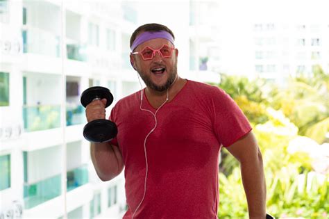 분홍색 티셔츠와 분홍색 안경을 쓴 장난꾸러기 뚱뚱한 남자가 체육관에서 피트니스에 종사하고 있습니다 체육관에서 물을 마시는 남자 T 셔츠에 대한 스톡 사진 및 기타 이미지