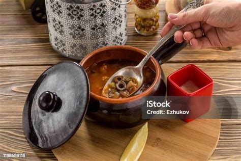 나무 테이블에 점토 냄비에 훈제 고기와 전통적인 러시아 수프 Solyanka의 숟가락을 들고 여성 손 건강한 식생활에 대한 스톡