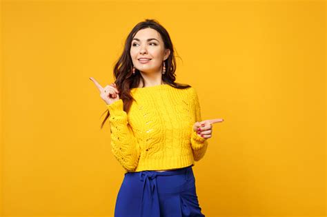 스웨터에 아름 다운 젊은 여자의 초상화 파란색 바지 찾고 노란색 오렌지 배경에 고립 된 옆에 인덱스 손가락을 가리키는 사람들은 진심으로 감정 라이프 스타일 개념입니다 복사