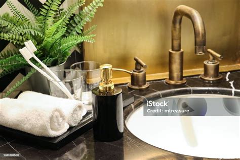 손 씻기를 위한 검은색 펌프 비누 디스펜서의 클로즈업 이미지 대리석 욕실 카운터 욕실 세면대 음료수 잔에 담긴 칫솔 롤링 플란넬 전경에 초점을 맞춘 금속 냄비에 있는 인공