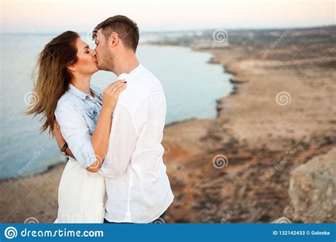 Het Jonge Paar Kussen Op De Rots Met De Spectaculaire Mening Over De Achtergrond Stock