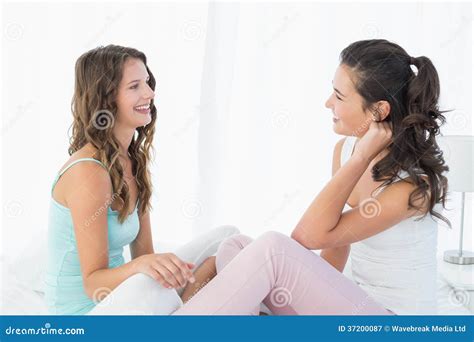 Het Gelukkige Jonge Vrouwelijke Vrienden Zitten Die Op Bed Babbelen Stock Afbeelding Image Of