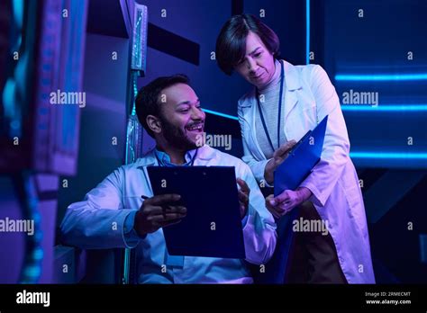 Hindu Male And Adult Female Scientists Analyze Data And Share Smiles In Neon Lit Science Center