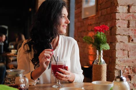 여자는 커피 숍에서 멀드 와인을 마신다 흰색 셔츠와 레스토랑 카페에서 알코올 레드 와인 한 잔을 들고 손톱에 적갈색 바니시에 세련된 소녀 곱슬 머리에 대한 스톡 사진 및