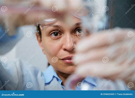 Female Laboratory Personnel Pouring Pink Liquid Chemical Substance From A Glass Flask Through A