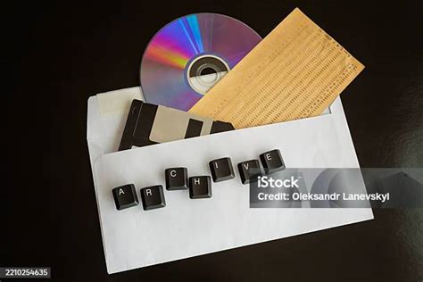 컴퓨터 키보드 키로 만든 Archive라는 단어가 적힌 흰색 봉투에 담긴 오래된 펀치 카드와 컴퓨터 플로피 디스크를 어두운