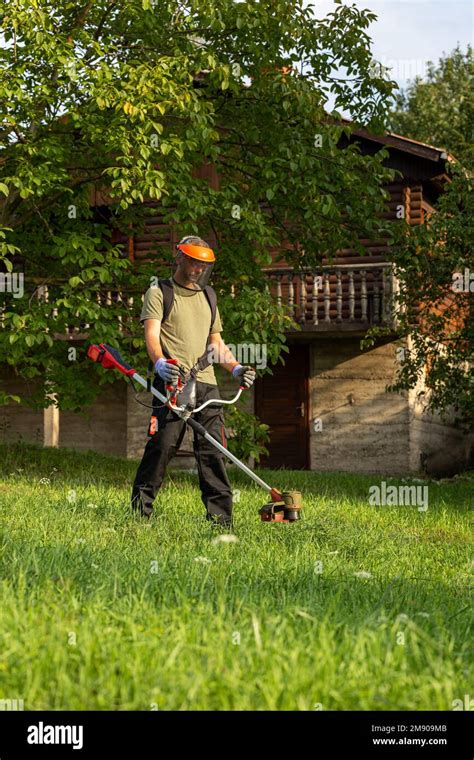 Landscape Maintenance Concept Man Cutting Grass In Yard By Using Electric String Grass Trimmer