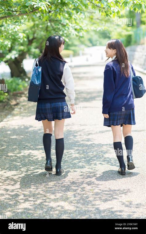 Two Japanese High School Girls Walking Down A Tree Lined Road Stock