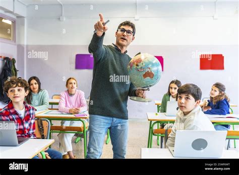 Geography Teacher Holding Globe And Pointing At Classroom Map While Teaching Geography To