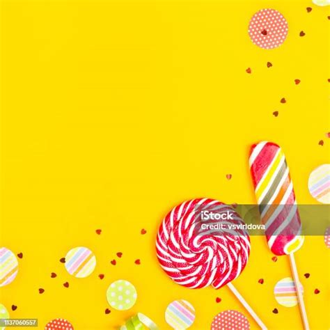 밝은 노란색 배경에 색종이 반짝이 및 축제 리본 종이 동그라미 사이에 두 개의 여러 가지 빛깔 캔디 평면도 평 신도 복사 공간 개념에 대한 스톡 사진 및 기타 이미지