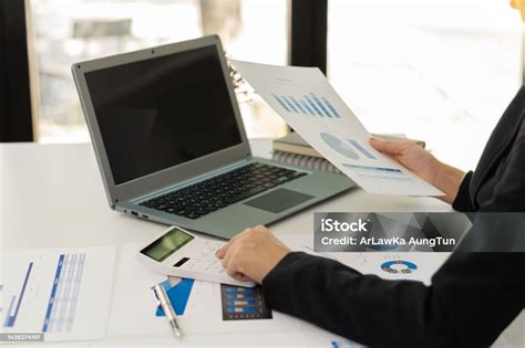 노트북 컴퓨터 및 문서에서 일하는 사무실에서 진지한 사업가 종이 그래프 보고서 차트를보고 최신 랩톱 컴퓨터로 그래프를 분석합니다