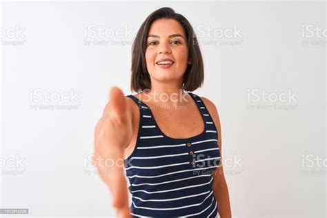 파란색 줄무늬 티셔츠를 입은 젊은 아름다운 여성은 인사와 환영으로 악수를 제공하는 친절한 미소 고립 된 흰색 배경 위에 서