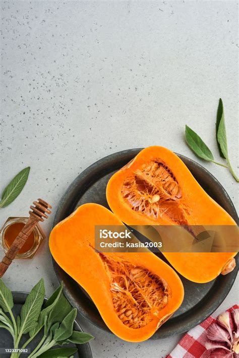 세이지 잎 여러 가지 빛깔의 후추 마늘 꿀 소금 후추를 흰 슬레이트 돌 또는 콘크리트 배경으로 곁들인 생 유기농 버터넛 스쿼시의 반쪽 음식 배경 복사 공간이 있는 상단