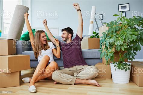 귀여운 젊은 커플 응원과 그들 주위의 상자와 함께 새 아파트에서 바닥에 앉아있는 동안 팔을 높이 새 집으로 이사에 대한 스톡