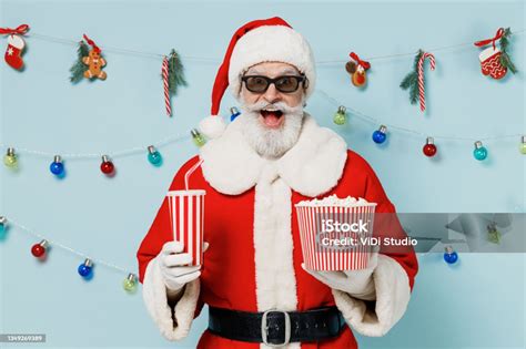 3d 안경을 쓴 젊은 노인 크리스마스 모자 빨간 정장 시계 영화 영화는 노란색 배경 스튜디오 초상화에 고립 된 소다 팝콘 컵의 양동이를 들고 있습니다 영화 라이프 스타일