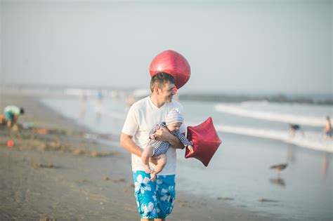 갓난아기 아들과 함께 해변에서 즐거운 시간을 보내는 쾌활한 젊은 아버지 공중에 아이를 던지는 아빠 2명에 대한 스톡 사진 및