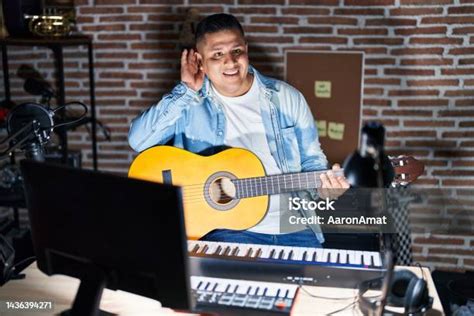 음악 스튜디오에서 클래식 기타를 연주하는 히스패닉 청년이 소문이나 가십을 듣고 귀에 손을 대고 웃고 있다 청각 장애 개념입니다 음악가에 대한 스톡 사진 및 기타 이미지