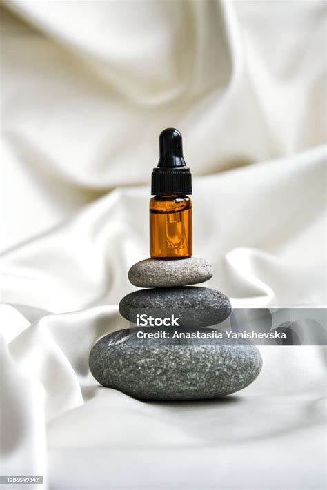 샴페인 사틴 직물 배경에 현무암 돌 더미에 세럼의 작은 병 트렌디 한 색상 자갈의 피라미드에 뷰티 파이펫 드롭퍼 갈색에 대한