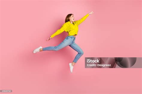 분홍색 배경에 뛰어 들어 기쁨과 흥분을 표현하고 캐주얼 한 노란색 스웨터와 청바지를 입고 활기찬 움직임과 생생한 색조의 트렌디 한 현대적인 의상을 보여주는 행복한 젊은 빨간