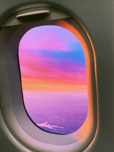 An Airplane Window Looking Out At The Sky And Clouds In The Distance With A Sunset Seen Through It