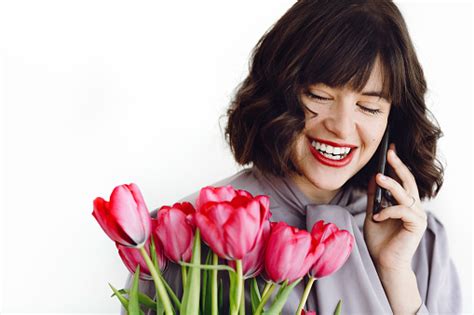 아름 다운 행복 소녀 공간 텍스트에 대 한 전화 및 흰색 배경 실내에 웃 고 잡고 빨간 튤립 얘기 붉은 입술과 꽃으로 세련 된 젊은 갈색 머리 여자 행복 한 일 공휴일에