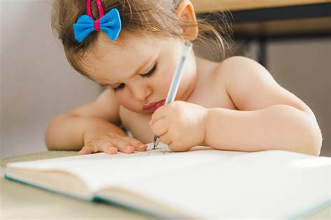 사랑스러운 백인 아기 소녀는 집 테이블에 앉아 노트북에 편지를 쓰기 위해 집중합니다 행복한 가족 아이 개념 교육 개념 행복 개념 학교 교육 행복한 가족 어린 시절 가족에