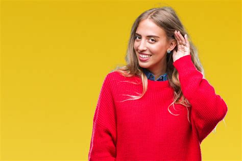 아름 다운 젊은 금발 여자 손으로 청각 소문 또는 험담을 듣고 귀에 웃 고 고립 된 배경 위에 겨울 스웨터를 입고 난청