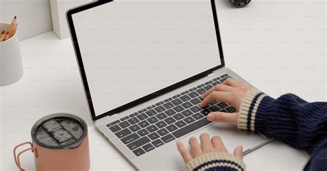 홈 오피스에서 얼음 커피 머그잔 책 문구류가 있는 흰색 책상에 있는 모형 노트북에 타이핑하는 여성 프리랜서의 자른 샷 사진 Unsplash의 사무실 이미지