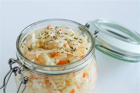 흰색 배경에 유리 항아리에 허브와 당근과 수제 소금에 절인 양배추 테이블에 자루가 있는 양배추절임 복사 공간을 복사합니다 통조림 식품의 개념 채식 음식 상단 보기복사 공간