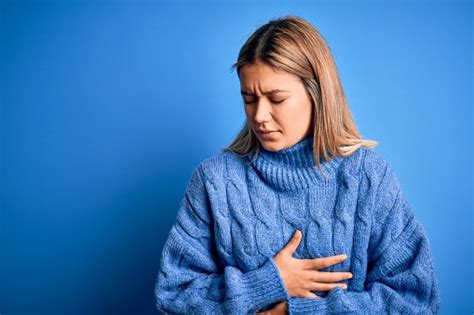 젊은 아름 다운 금발 여자 겨울 울 스웨터를 입고 푸른 고립 된 배경 위에 손에 위장에 소화 불량 고통 스러운 질병 기분이 좋지 않습니다 아쉬 컨셉 건강관리와 의술에 대한