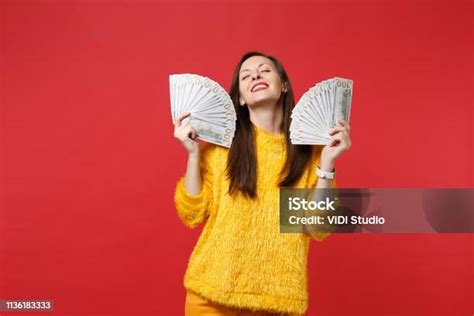 닫힌 눈이 달러 지폐에 돈의 팬을 들고 모피 스웨터에서 편안한 젊은 여자 현금 돈은 빨간색 배경에 고립 사람들은 진심으로 감정 라이프 스타일 개념입니다 복사 공간을 모의