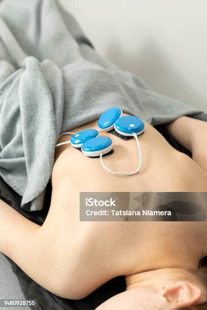 뇌성 마비가있는 백인 환자 소파에 누워있는 척추 측만증 무선 전기 근육 자극기 마사지 여성의 등 통증 치료 재활 의료 장비 수직 평면 건강관리와 의술에 대한 스톡 사진 및