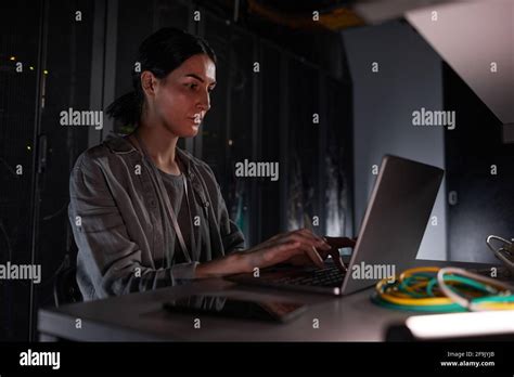 Portrait Of Female Network Engineer Using Laptop While Sitting In Dark Server Room Copy Space