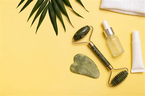 옥 돌 얼굴 롤러 마사지 및 화장품 오일과 수건으로 미용 얼굴 마사지 치료 노란색 배경에 평평한 누워 건강관리와 의술에 대한