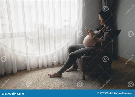 Young Asian Pregnant Woman Using Mobile Phone In Living Room Stock