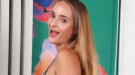 A Woman With Long Blonde Hair Standing In Front Of A Poster