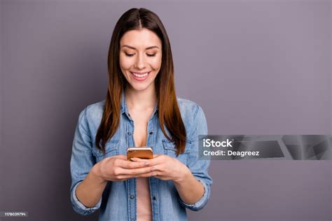 긍정적 인 쾌활한 여자의 초상화 사용 그녀의 휴대 전화 읽기 뉴스 Scoail 계정 느낌 재미 착용 데님 청바지 셔츠 회색 색상 배경 위에 고립 Brand Name