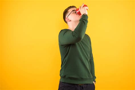 노란 배경에 빨간 플라스틱 컵에서 마시는 녹색 스웨터에 젊은 잘생긴 자신감 남자의 초상화 개념에 대한 스톡 사진 및 기타 이미지 개념 관능 광고 Istock