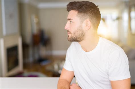 젊은 잘생긴 남자 캐주얼 흰색 T 셔츠를 입고 집에서 측면을 찾고 자신감 미소와 함께 자연 스러운 얼굴로 프로필 포즈를 휴식 T