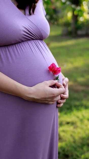 Premium Photo Midsection Of Pregnant Woman Holding Flower On Belly In Park