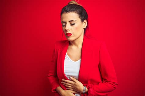 소화 불량 고통스러운 질병이 좋지 않아 위장에 손을 들고 빨간 고립 된 배경 위에 서있는 젊은 아름다운 비즈니스 여성 아쉬 컨셉 갈색 머리에 대한 스톡 사진 및 기타 이미지