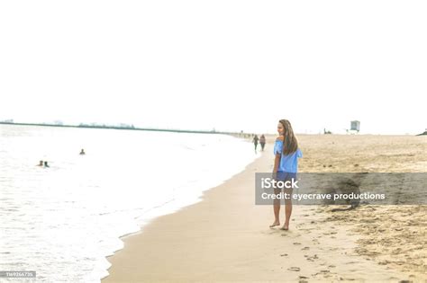 긴 갈색 물결 모양의 머리를 가진 젊은 밀레니엄 필리핀 여성은 파도와 서핑 보드를 들고 물 근처 바다의 가장자리에 모래를 걷고 캘리포니아에서 물 해변을 즐기고 20 29세에