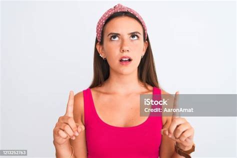 분홍색 캐주얼 티셔츠와 고립 된 흰색 배경 위에 디아뎀을 입은 젊은 아름다운 소녀는 손가락과 팔을 들고 위를 올려다 보고 놀랐습니다 T 셔츠에 대한 스톡 사진 및 기타