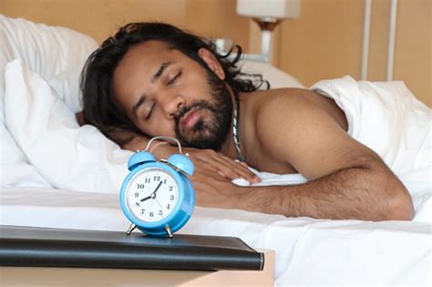 블루 메탈 케이스 복고풍 알람 시계 더블 벨 야간 스탠드에 앉아 있는 흰색 다이얼이 있는 아날로그 디스플레이 시계 베개에 누워 있는 인도 남자 전경에 초점을 맞춘 30 34