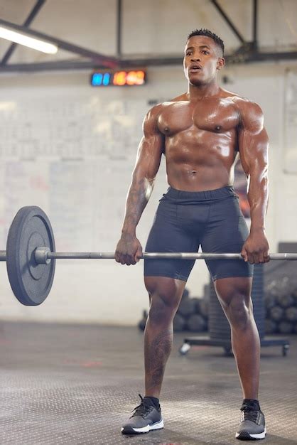 フィットネスの筋肉と、物理的なトレーニング ルーチン中にジムでバーベルを持つ黒人男性のボディービルダースポーツ センターでウェイトを持ち上げる上半身裸の男性アスリートと強く運動し、汗をかく