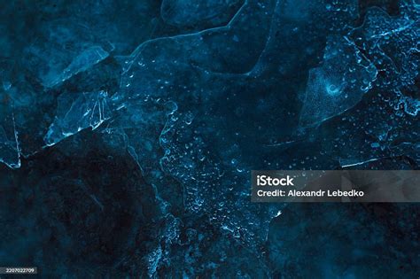 짙은 푸른 색조의 추상적인 얼음 패턴을 클로즈업하여 복잡한 질감과 거품을 보여줍니다 이 이미지는 겨울 자연의 예술성과 얼어붙은