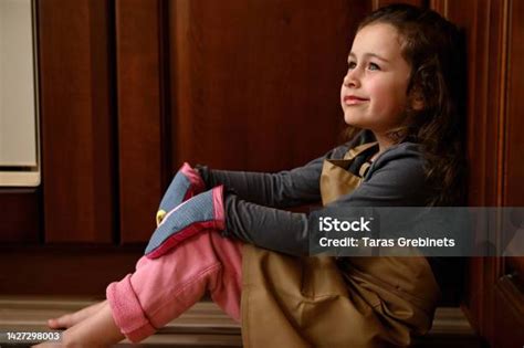 베이지 색 요리사 앞치마와 주방 장갑을 착용하고 바닥에 맨발로 앉아 꿈꿔 보며 꿈꿔 보는 사랑스러운 어린 소녀 4 5세에 대한 스톡 사진 및 기타 이미지 Istock