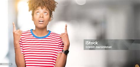 격리 된 배경 위에 아름 다운 젊은 아프리카계 미국인 여자 놀라게 했 고 올려 손가락으로 가리키는 그리고 팔 놀 랐 어 요 T 셔츠에 대한 스톡 사진 및 기타 이미지