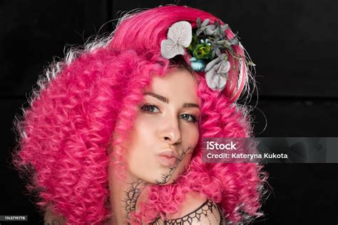 아프리카 스타일 곱슬 밝은 분홍색 머리와 젊은 매력적인 백인 여자 모델의 초상화 문신 얼굴과 꽃 그녀의 머리에 짠 검은 배경에 스튜디오에서 사진 감정에 대한 스톡 사진 및